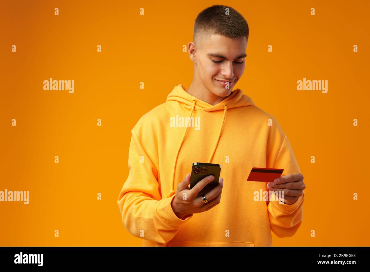 Young man holding credit card and smartphone against yellow background ...