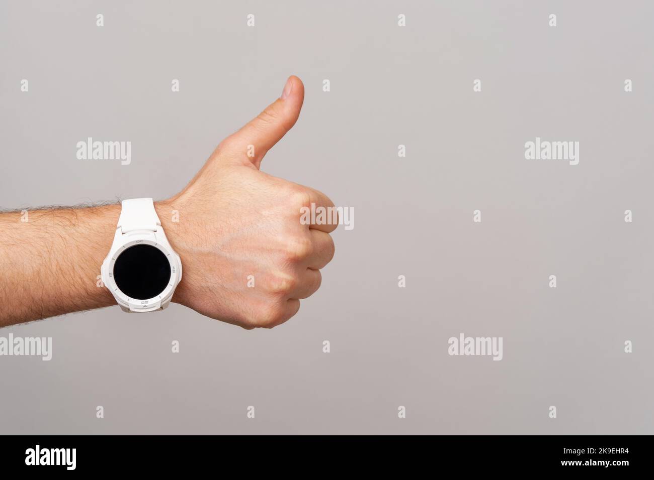 Photo of male hand with smartwatch showing thumb up gesture over grey ...