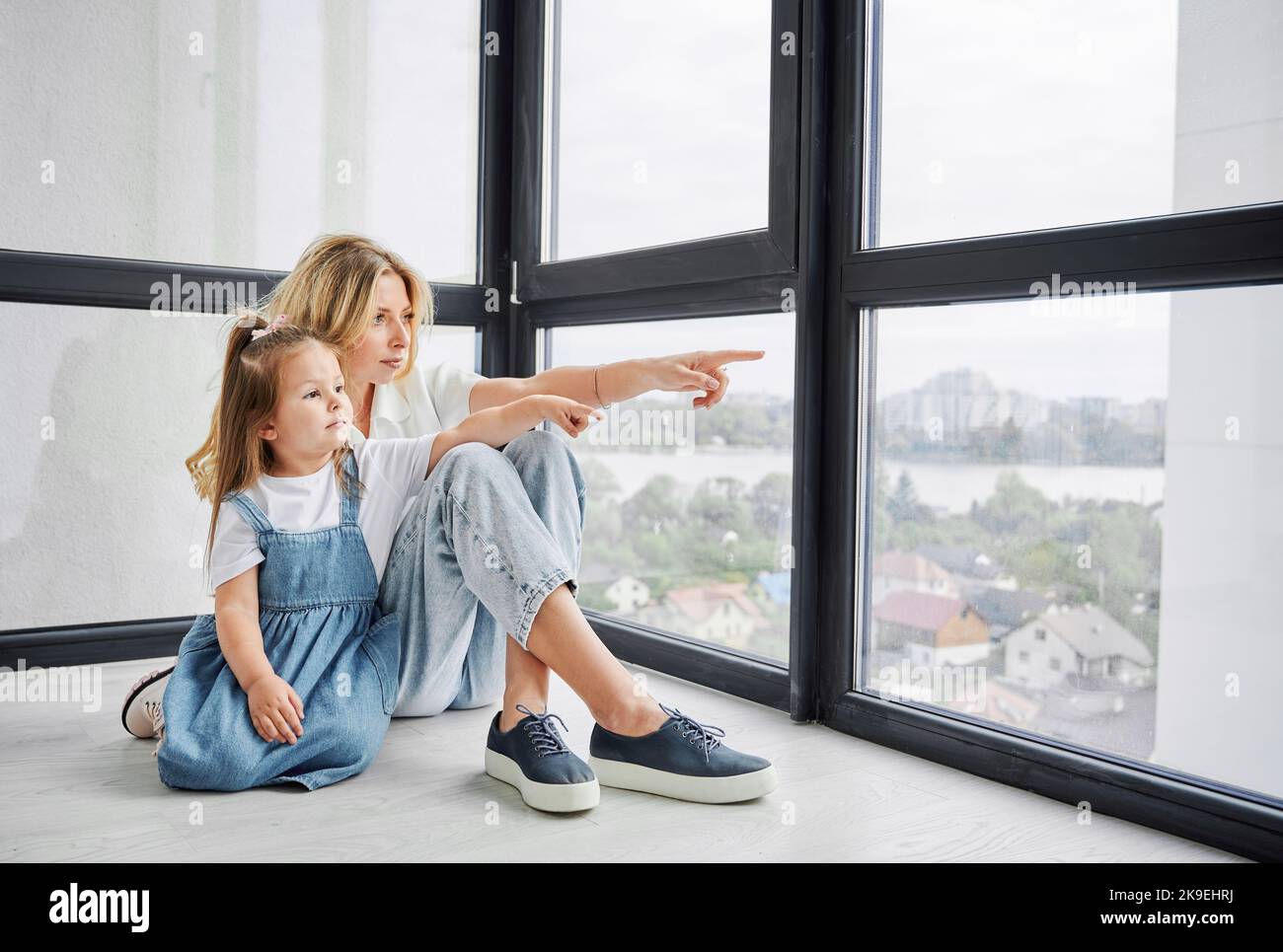 Woman and little girl sitting on the floor and looking and pointing out ...