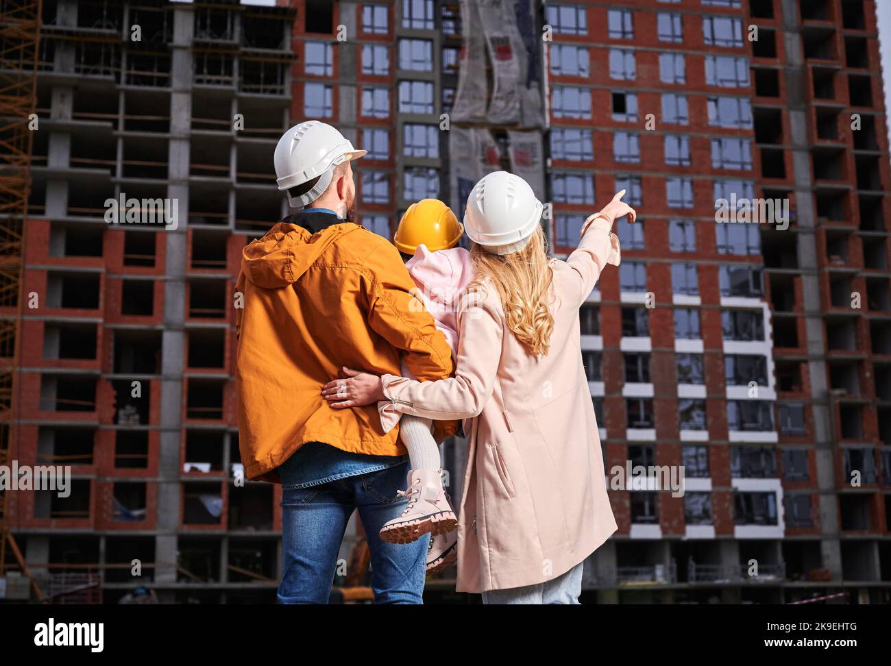Back view of woman pointing at apartment building under constructing while standing next to ...