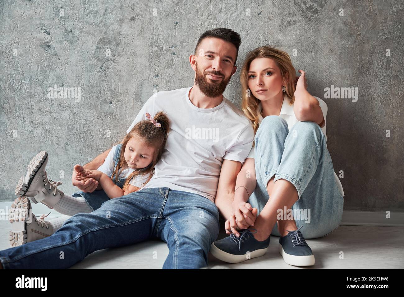 Loving parents and little child sitting by the wall in new apartment ...