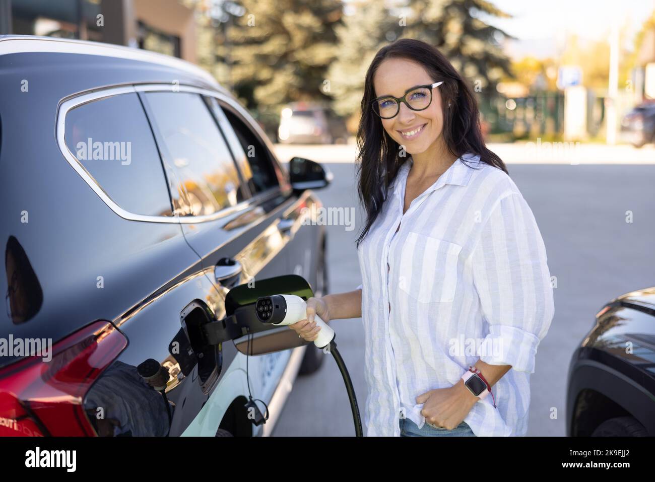 A young beautiful woman is charging her electric car in a charging ...