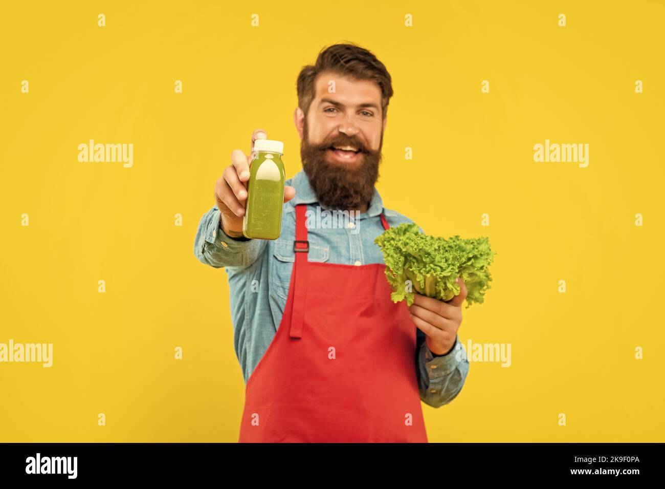 Happy man giving juice bottle holding fresh lettuce yellow background ...