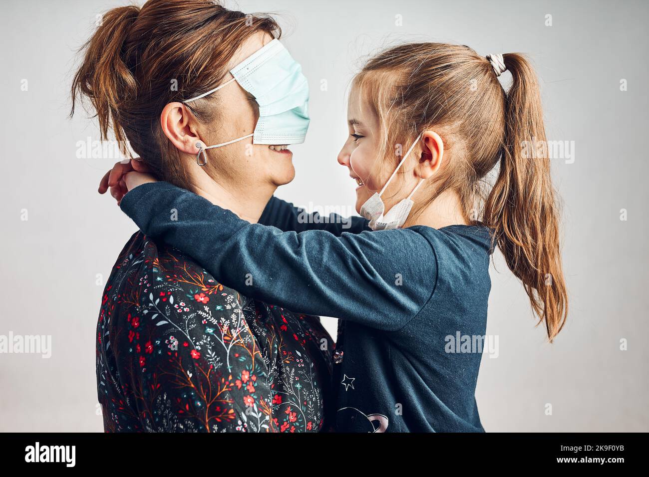 Little girl kissing her mother who has covered eyes with face mask for ...