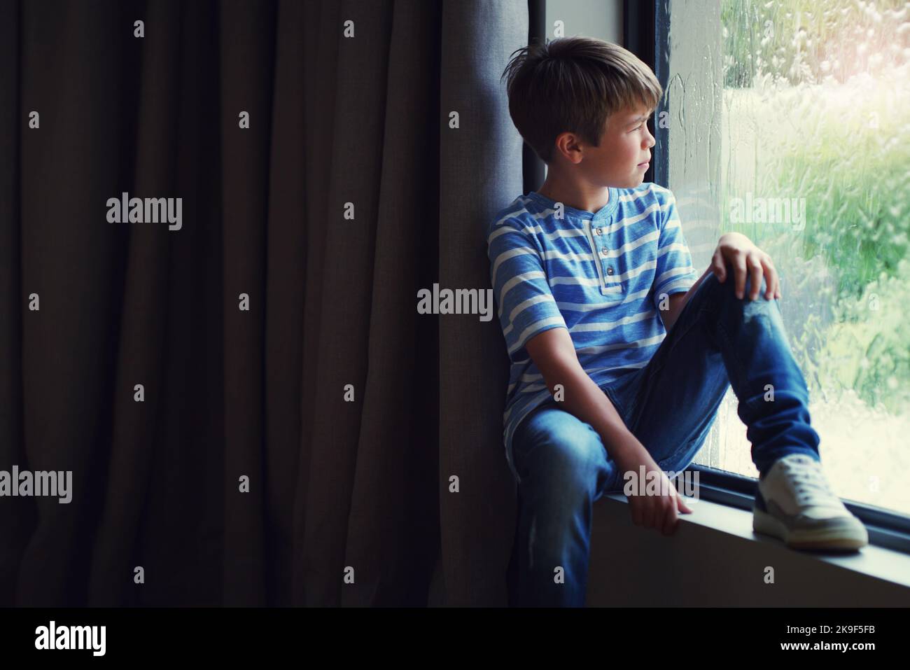 Rain, go away so I can go outside and play. a sad young boy watching ...