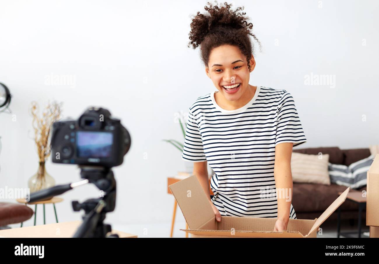 Young woman unpacking boxes on camera. African American female small ...