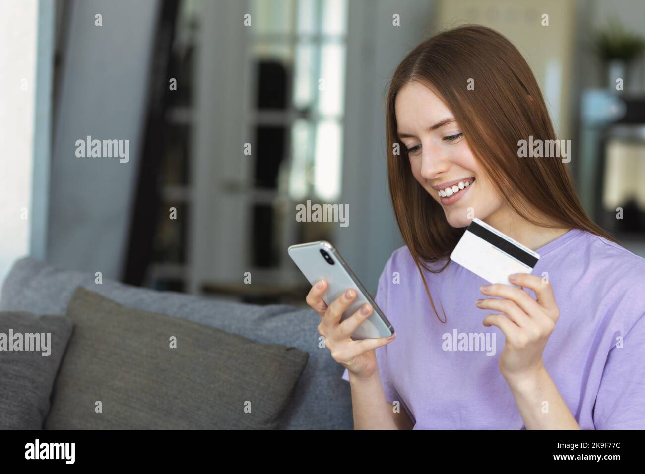 Happy smiling female holding credit card, looking at smartphone screen ...