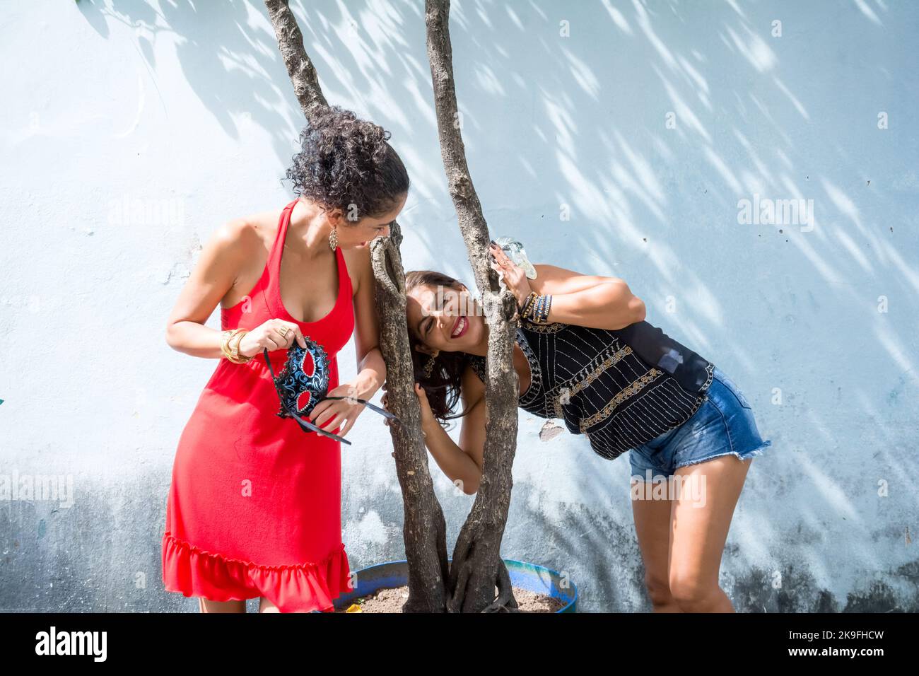 Portrait of two girls between a tree branch against a light blue wall ...