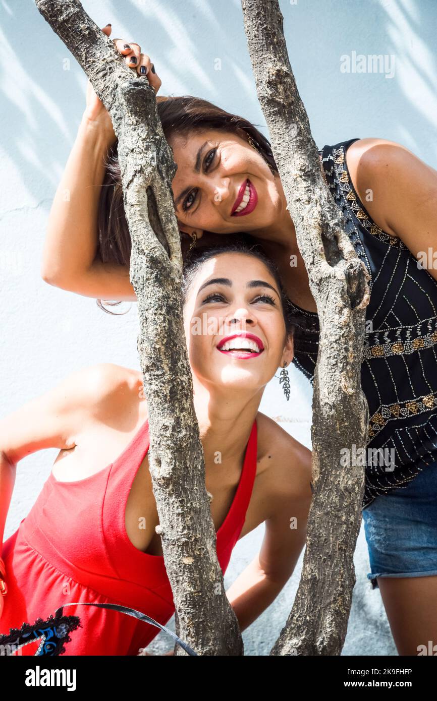 Portrait of two girls between a tree branch against a light blue wall ...