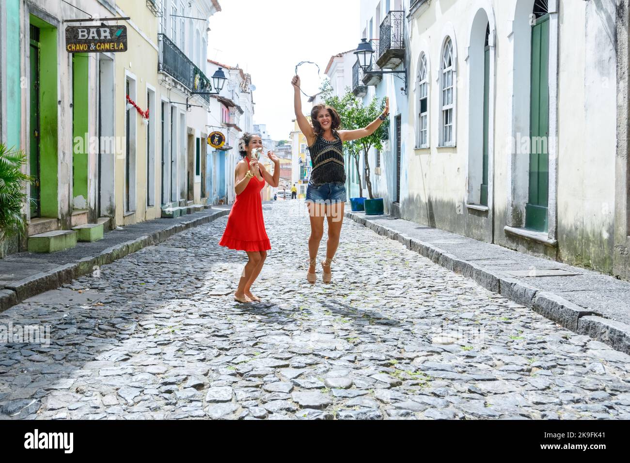 Portrait of two beautiful and happy girls jumping on the cobblestone ...