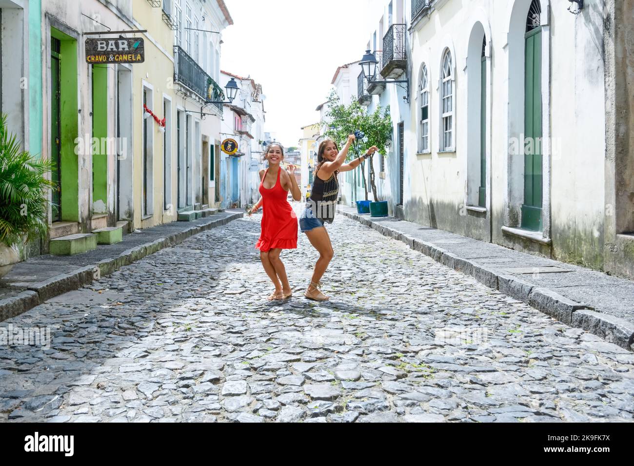 Portrait of two beautiful and happy girls jumping on the cobblestone ...