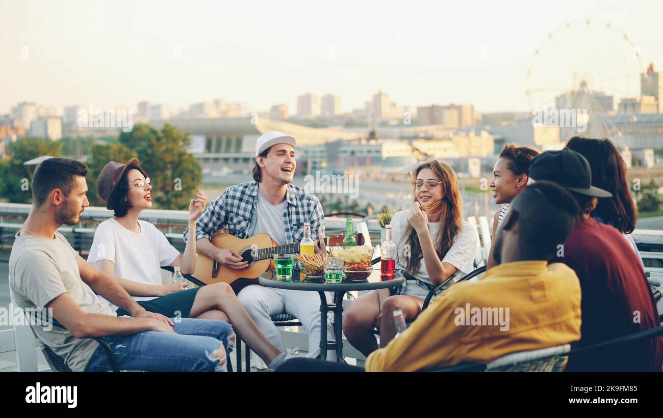 Joyful male musician is playing the guitar with his friends singing and ...