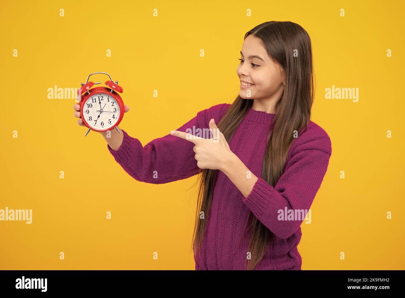 Excited face. Teenager child hold clock isolated on yellow studio ...