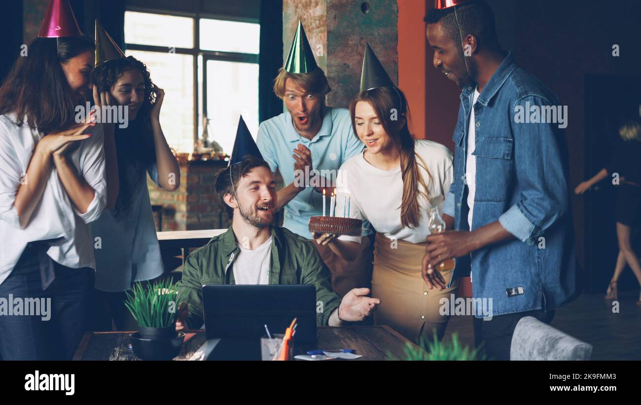 Young man is working in office when his colleagues are bringing him ...