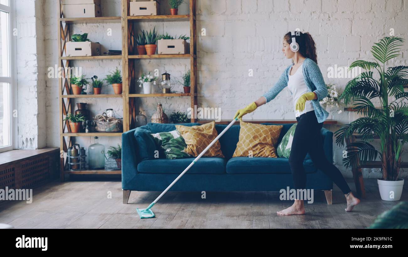 Cheerful young woman is dancing with mop during routine clean-up in ...