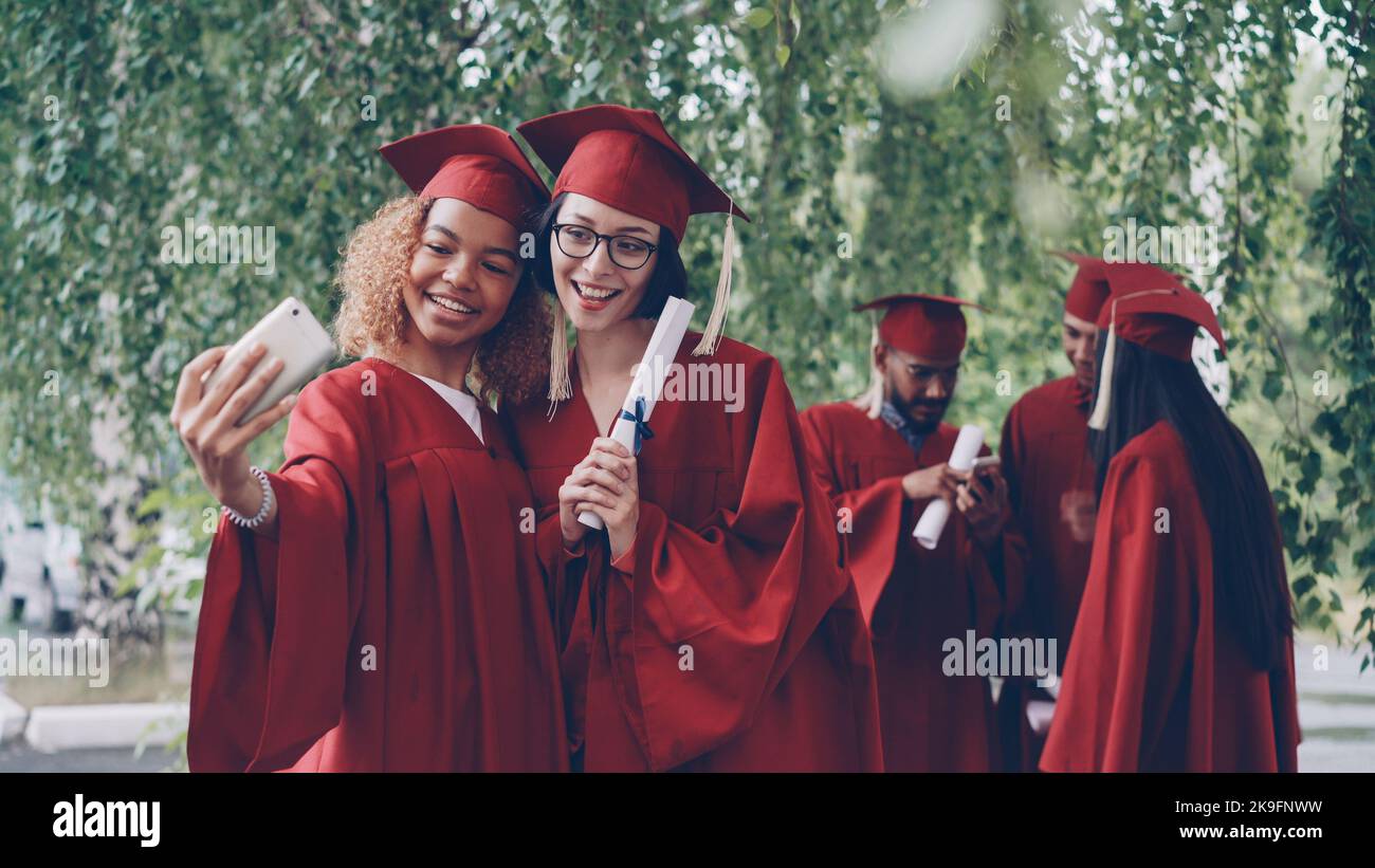 Pretty female graduates are taking selfie with diploma scroll using ...