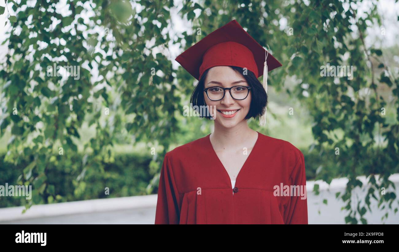Portrait of joyful young woman graduating student in red gown and ...