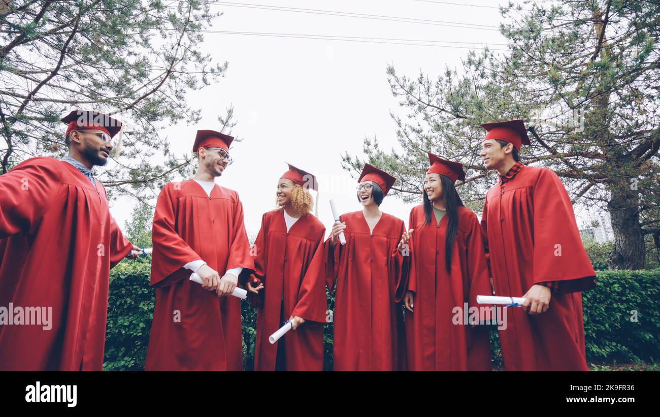 happy graduates laughing and celebrating graduation on college campus ...