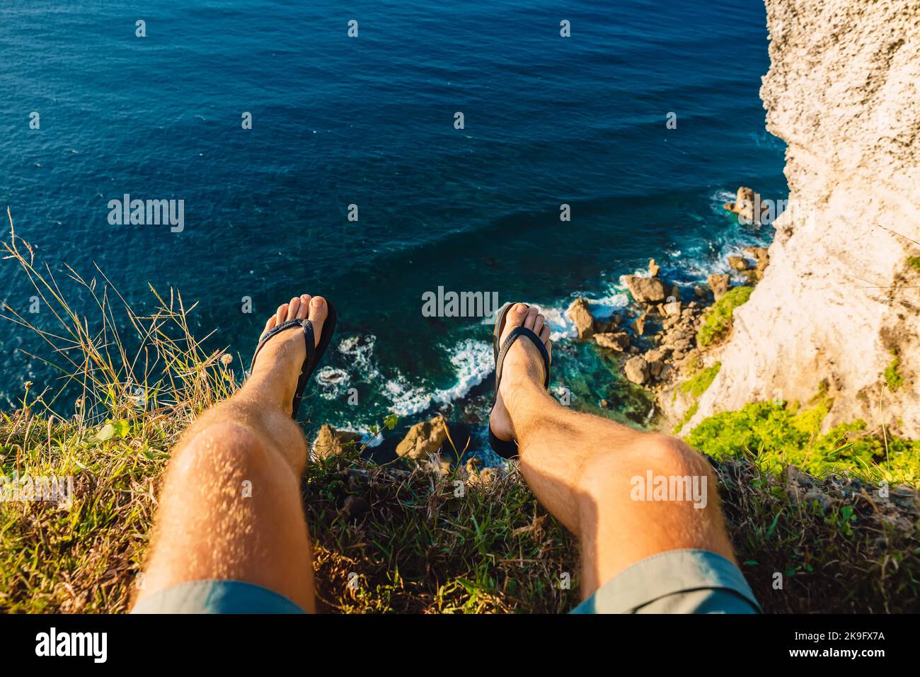 Legs of men on rocky cliff over ocean with waves Stock Photo - Alamy