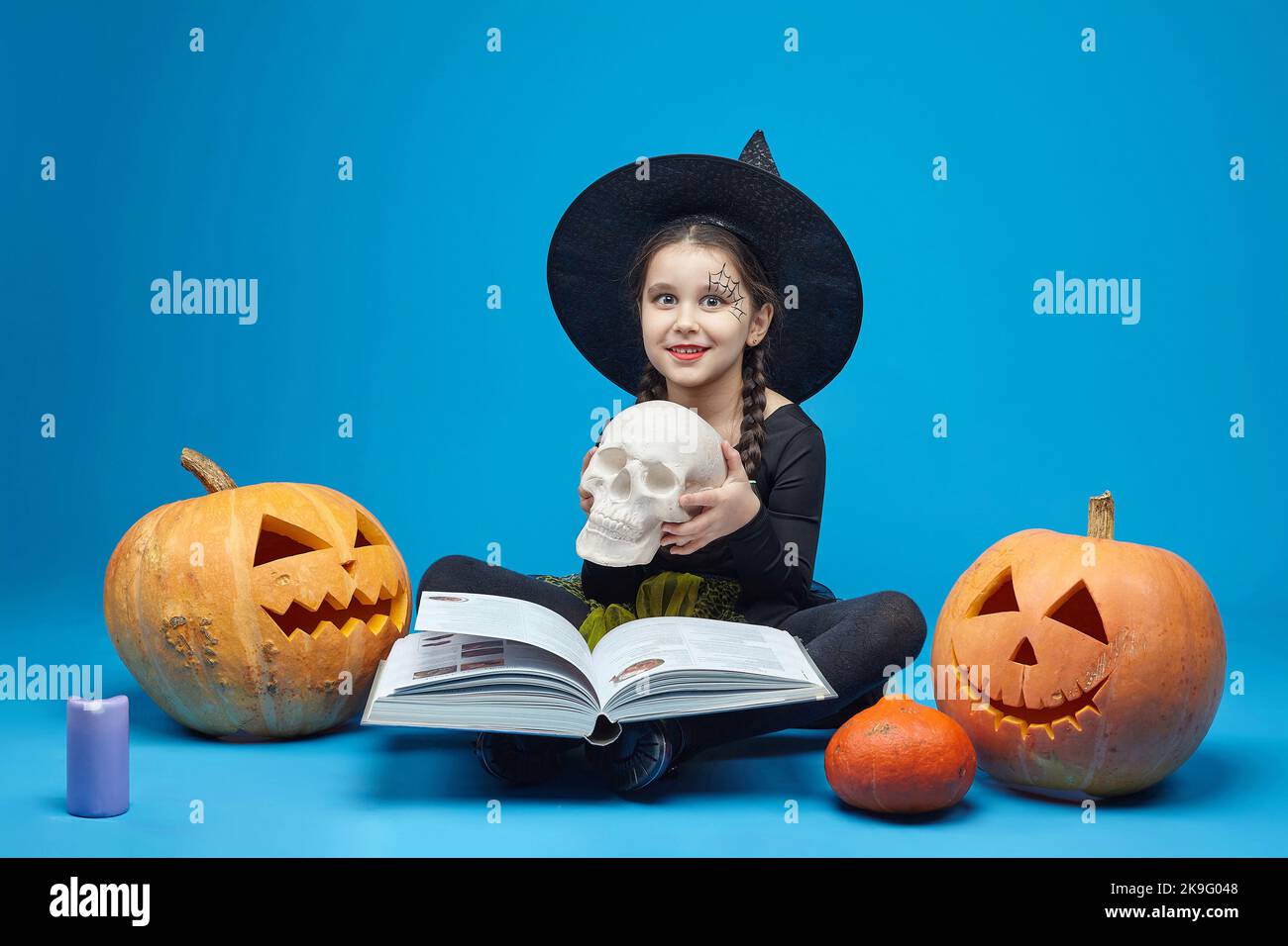 charming little girl in a witch costume holds a skull in her hands ...
