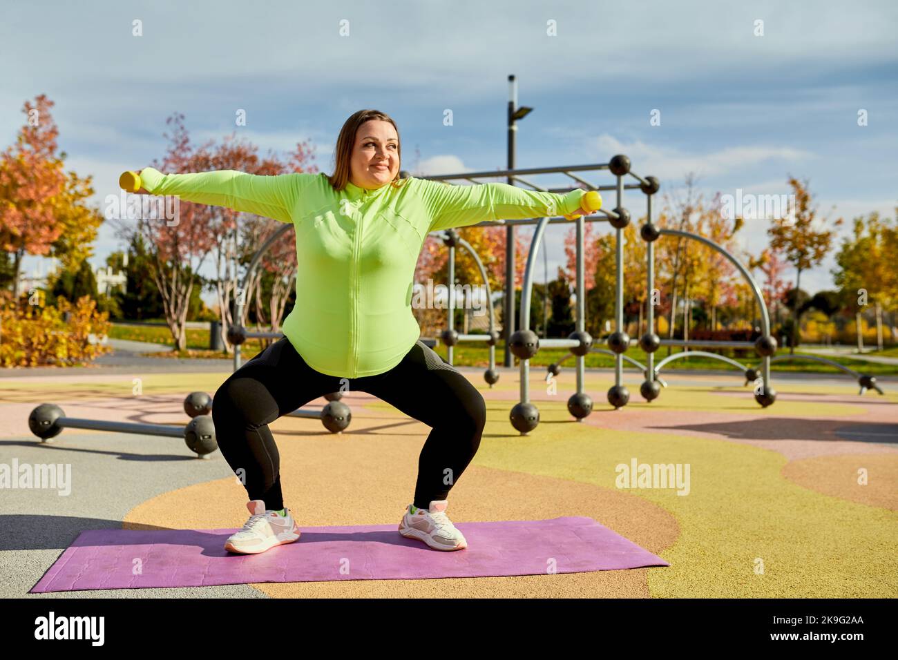 Happy overweight young woman doing fitness exercises at street public ...