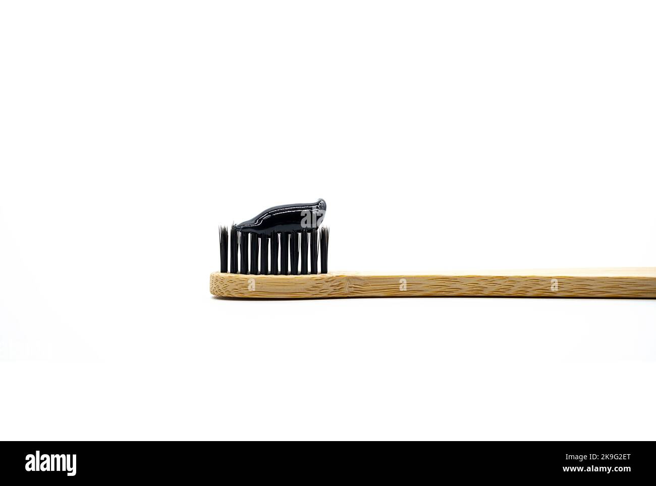 Whitening black charcoal toothpaste on bamboo toothbrush, close up. Eco ...