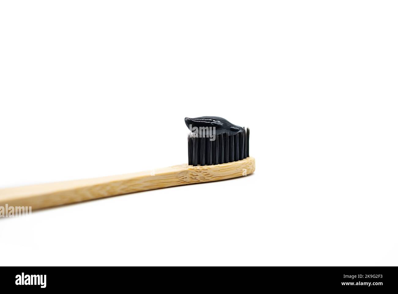 Whitening black charcoal toothpaste on bamboo toothbrush, close up. Eco ...