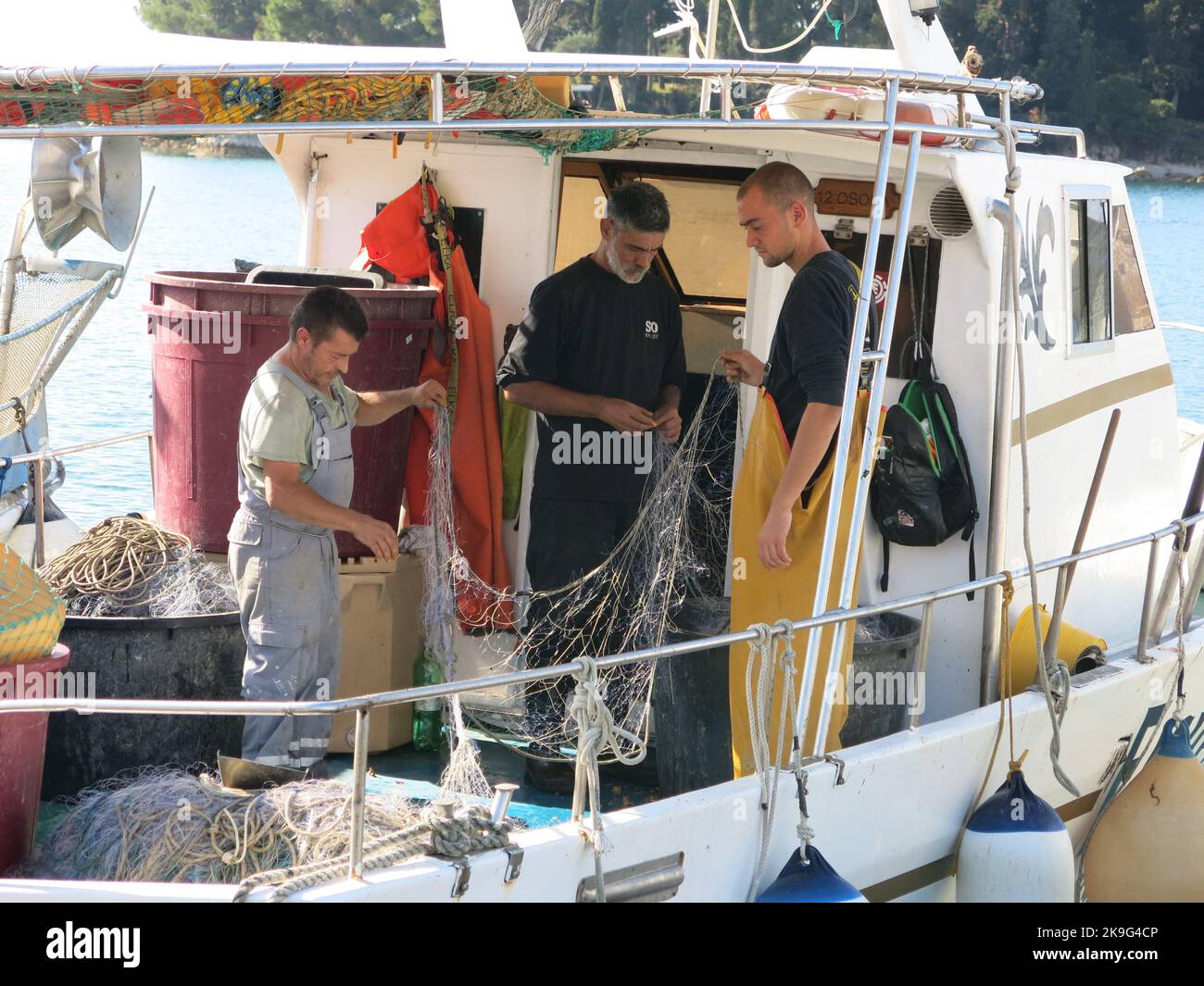 Three fishermen are untangling their nets on board their fishing boat ...