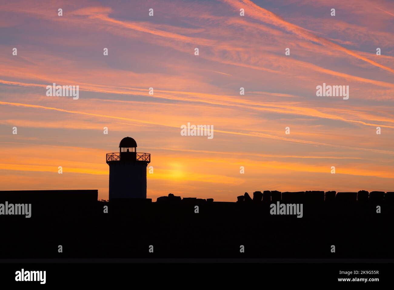 Burry Port Lighthouse silohetted in the morning sunrise with a streaky ...
