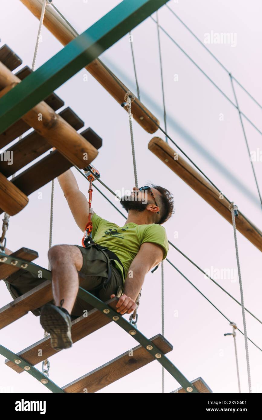 Handsome man balancing himself on the ladder in the adventure park ...