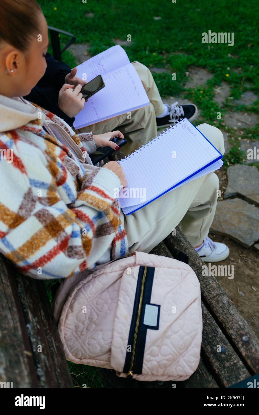 Female high school friends writing their homework together, outdoors ...