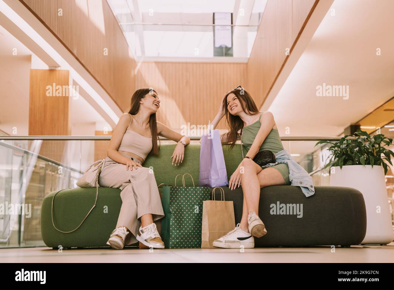 Young beautiful friends together at the mall sitting on a couch and ...