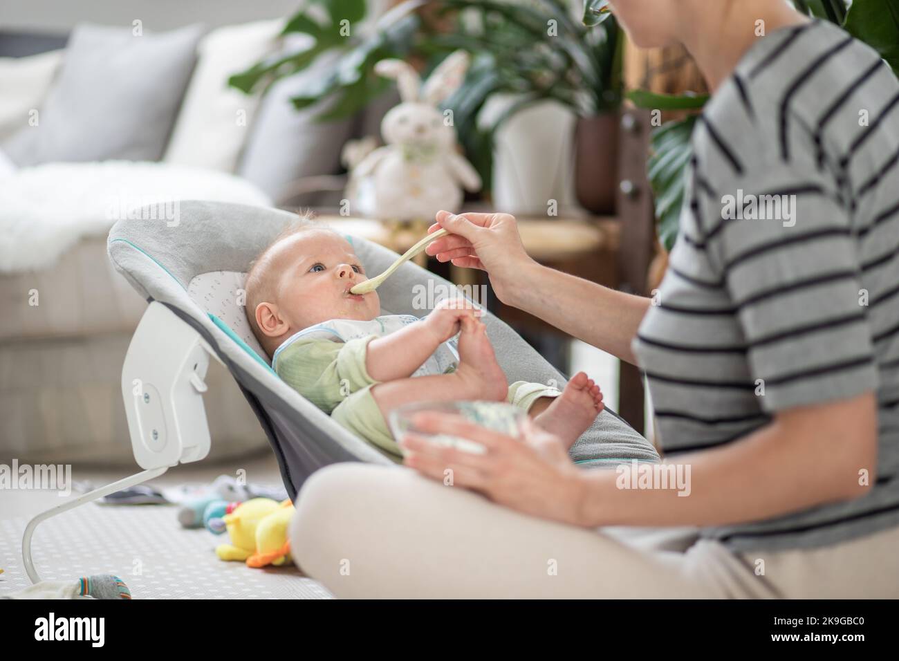 Mother spoon feeding her baby boy infant child in baby chair with fruit ...