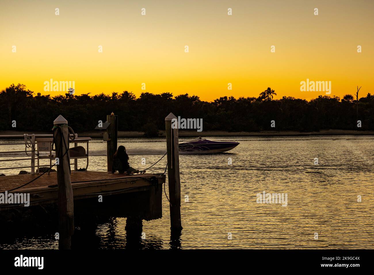 A girl watching the sunset on a dock as a speed boat goes by Stock ...
