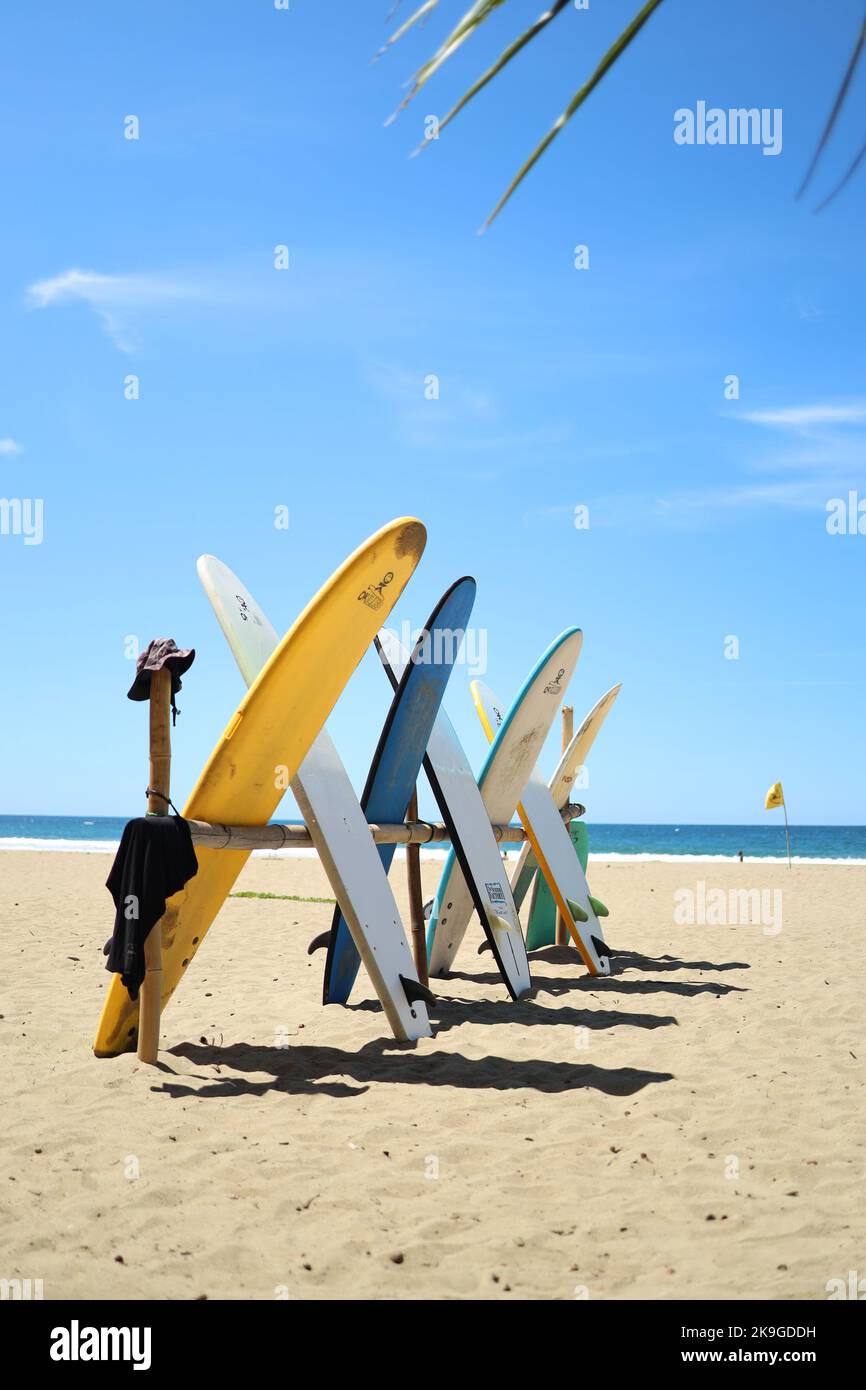 A vertical shot of unfiltered surfboards on the sandy beach with blue ...