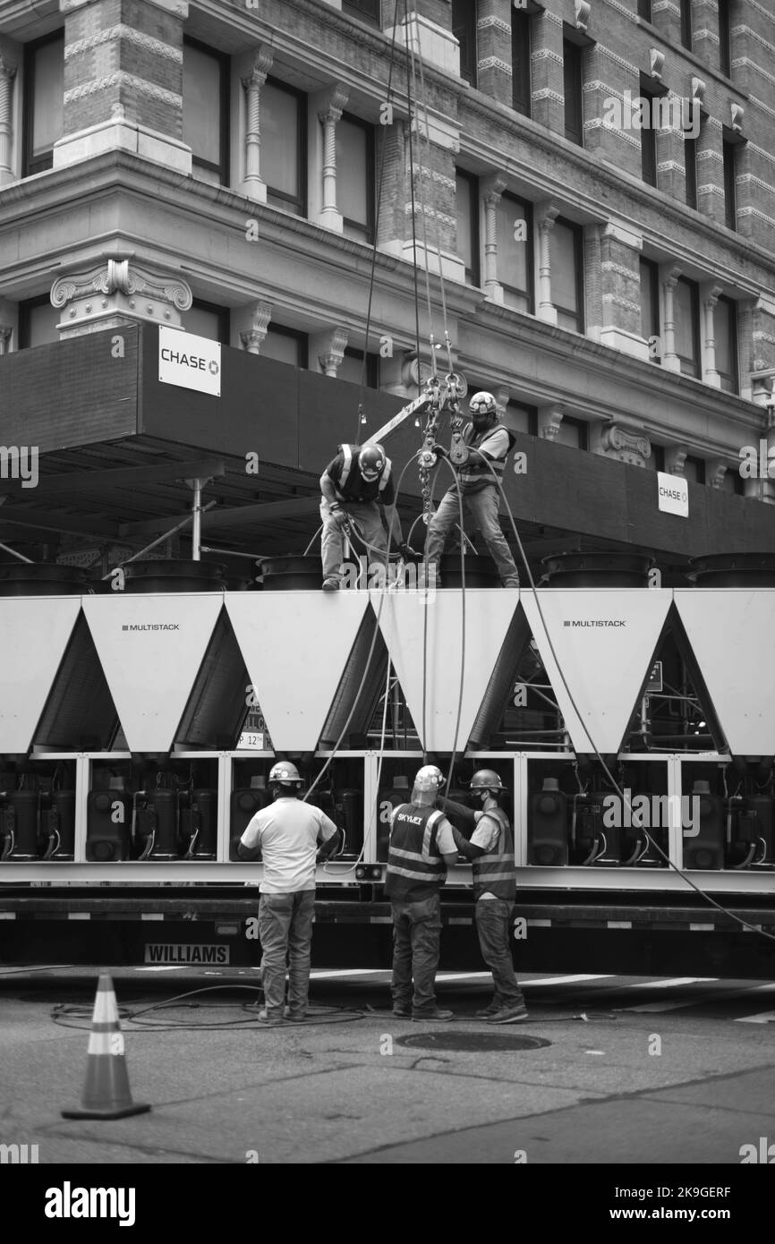 A grayscale shot of construction workers lifting object with crane in ...