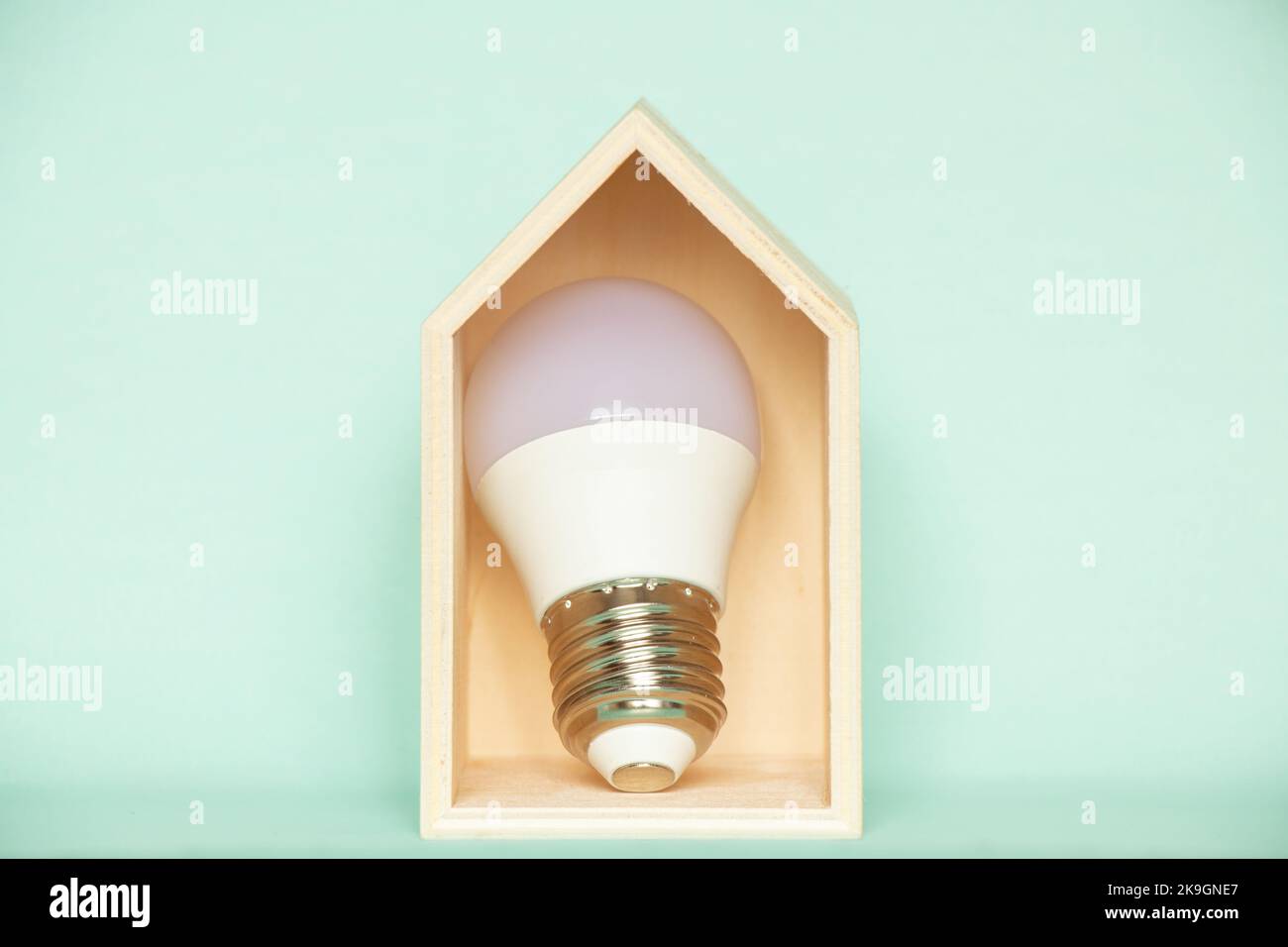The LED light bulb lies in a small wooden house on a blue background ...