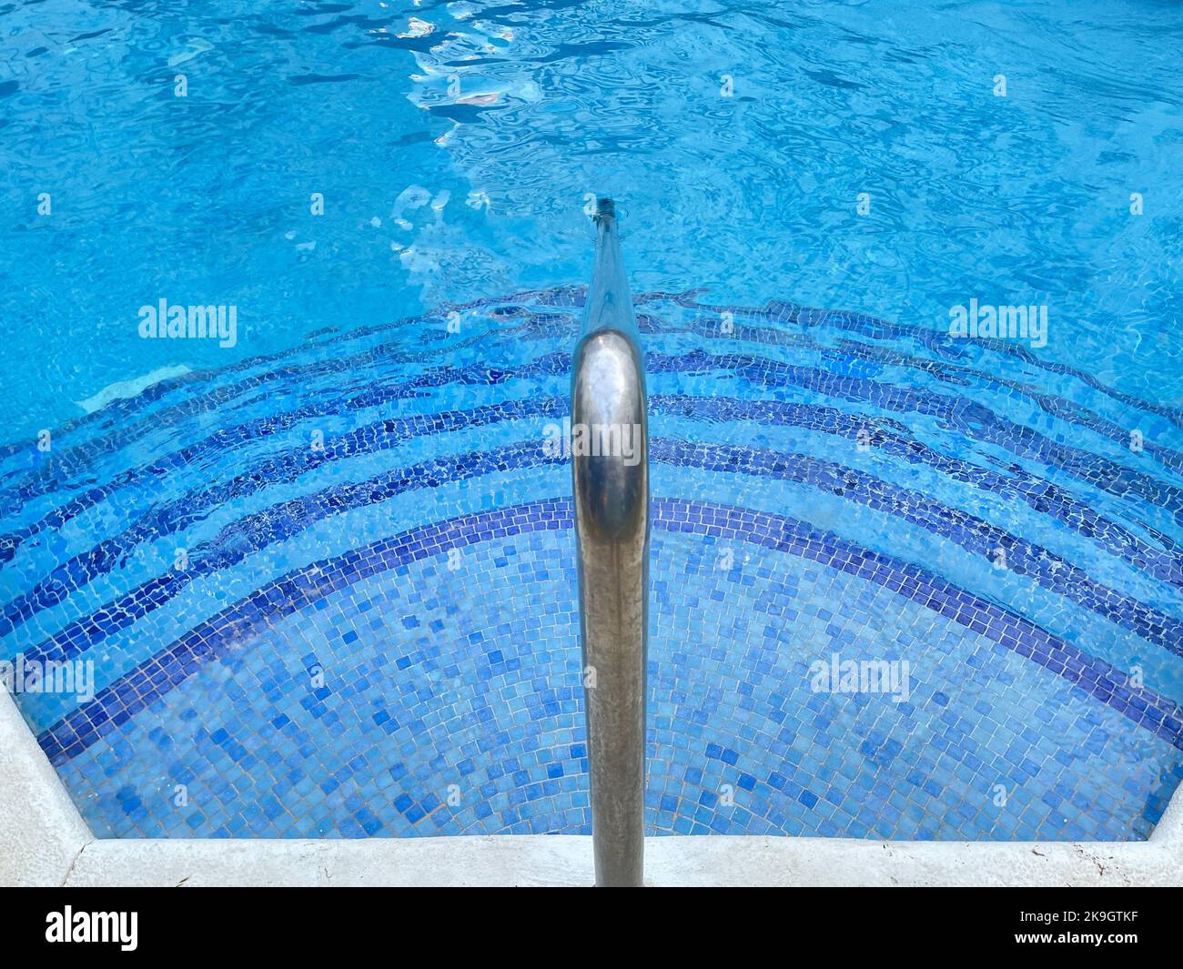 A selective of stainless steel handrail descending in clear pool water ...
