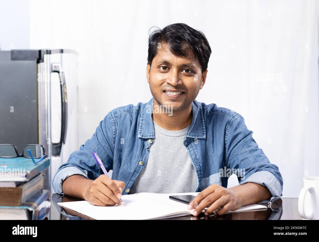 An Indian young male looking at camera with smiling face while studying ...
