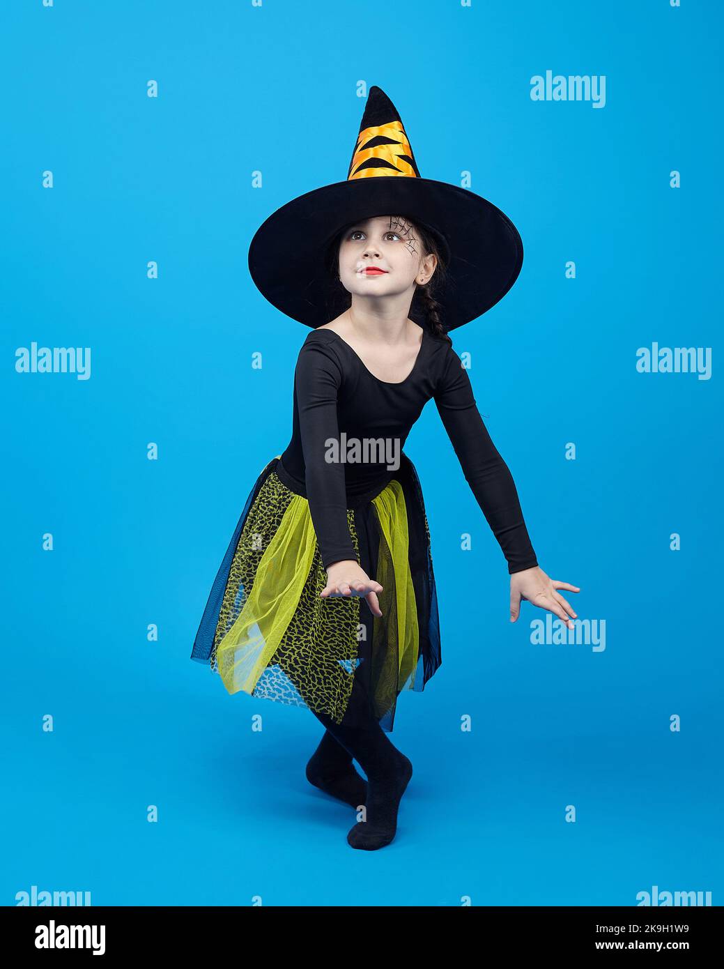 charming little girl in a witch costume dancing in the studio on a blue ...