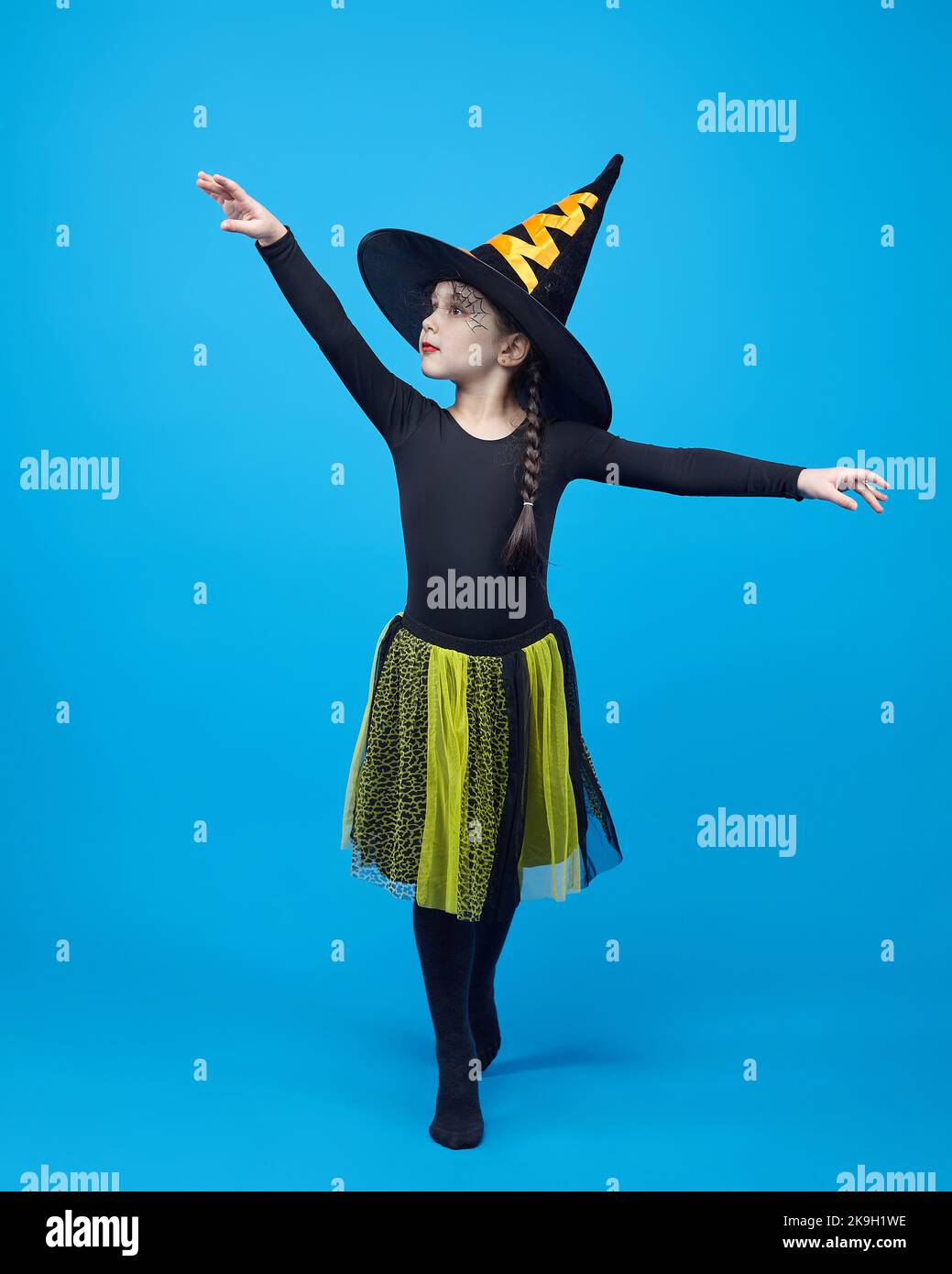 charming little girl in a witch costume dancing in the studio on a blue ...