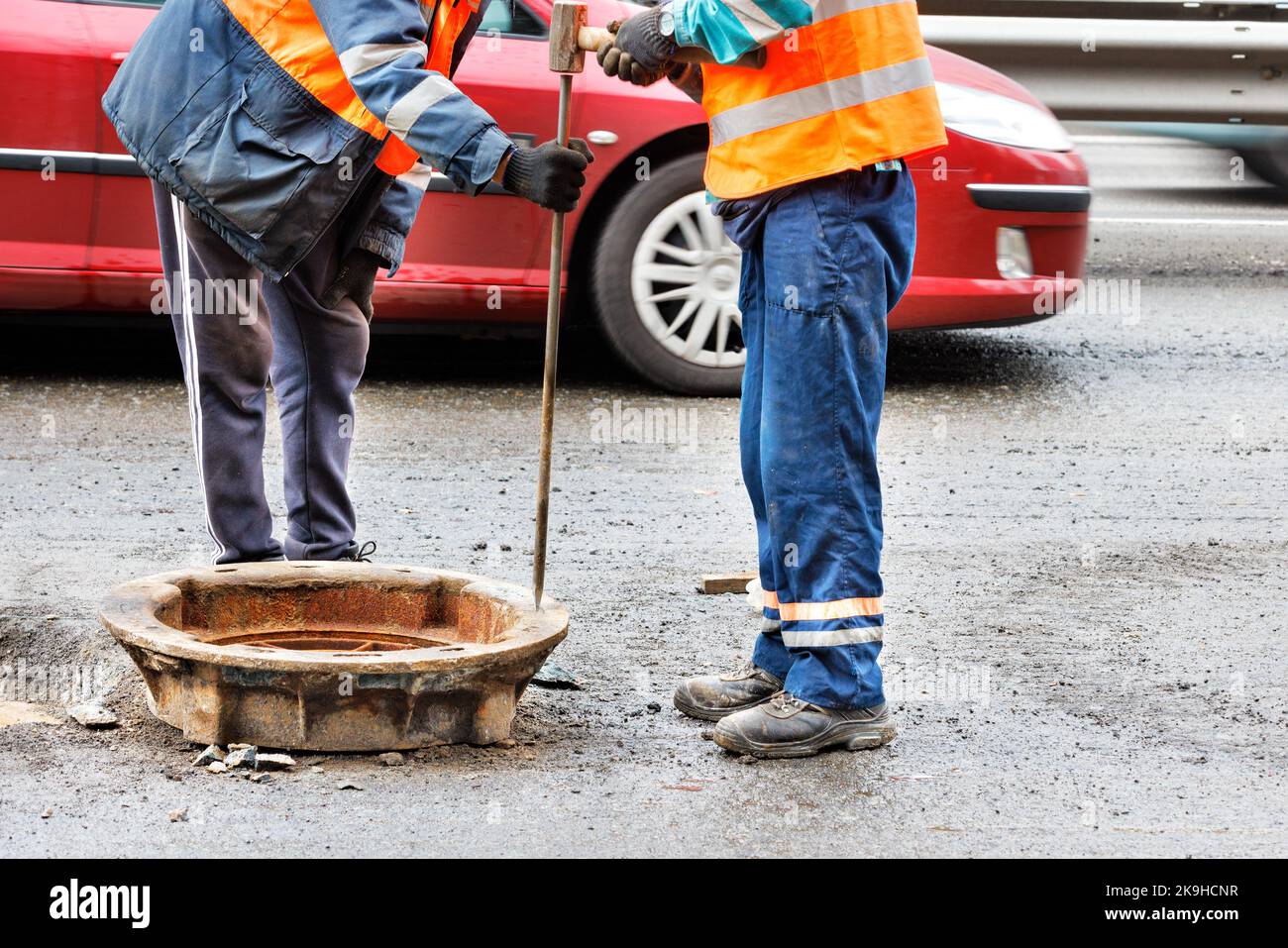 Road workers in orange overalls are repairing an old sewer manhole on ...
