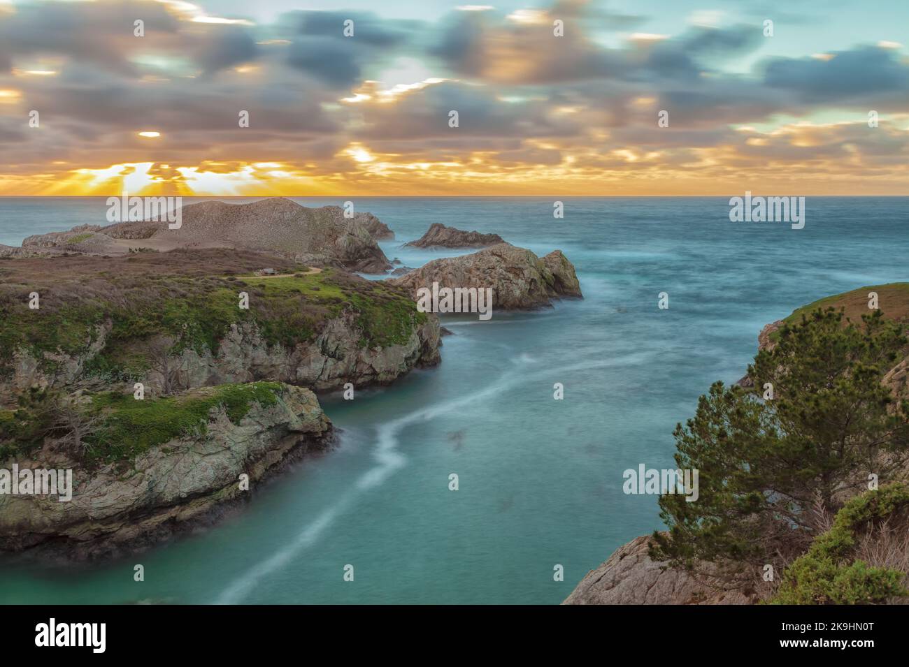 The image captures a breathtaking sunset over a rugged coastline at ...