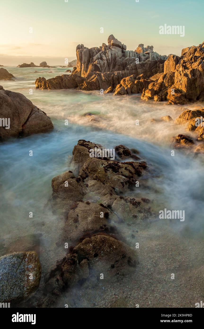 A serene landscape photograph captures a rocky coastline bathed in the ...