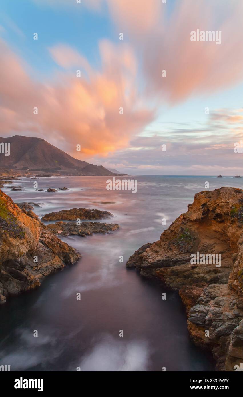 A serene coastal scene at sunset showcasing rugged, brown cliffs rise ...