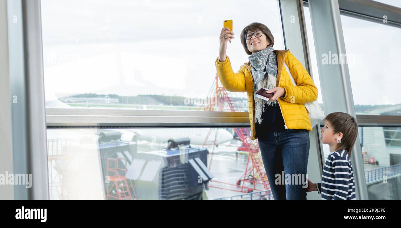 Son waits while mother makes selfie on her smartphone in airport ...