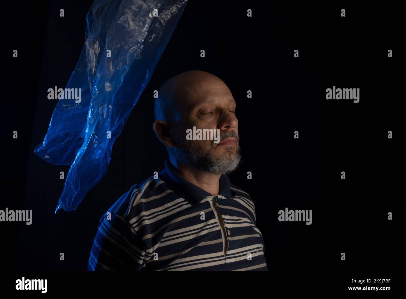 Mature man with a transparent plastic blue bag flying over his head and ...
