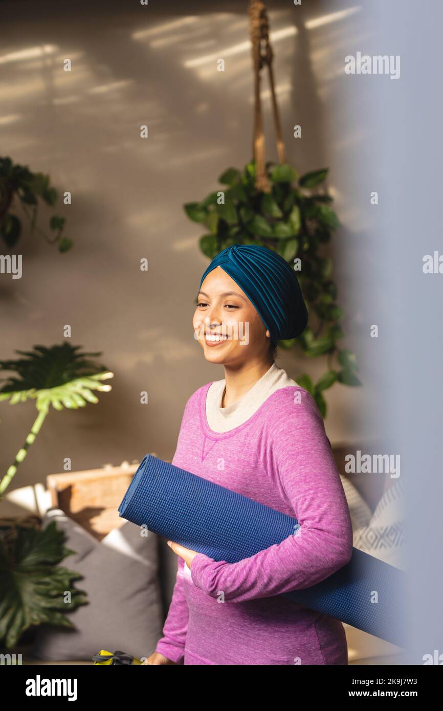 Happy biracial woman wearing hijab, holding yoga mat and smiling in ...
