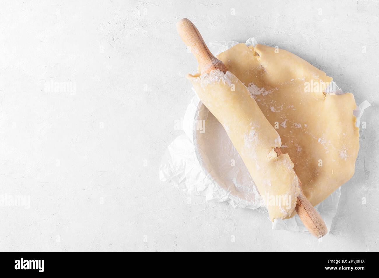 Raw crust pie dough into a baking dish with a rolling pin on a light ...