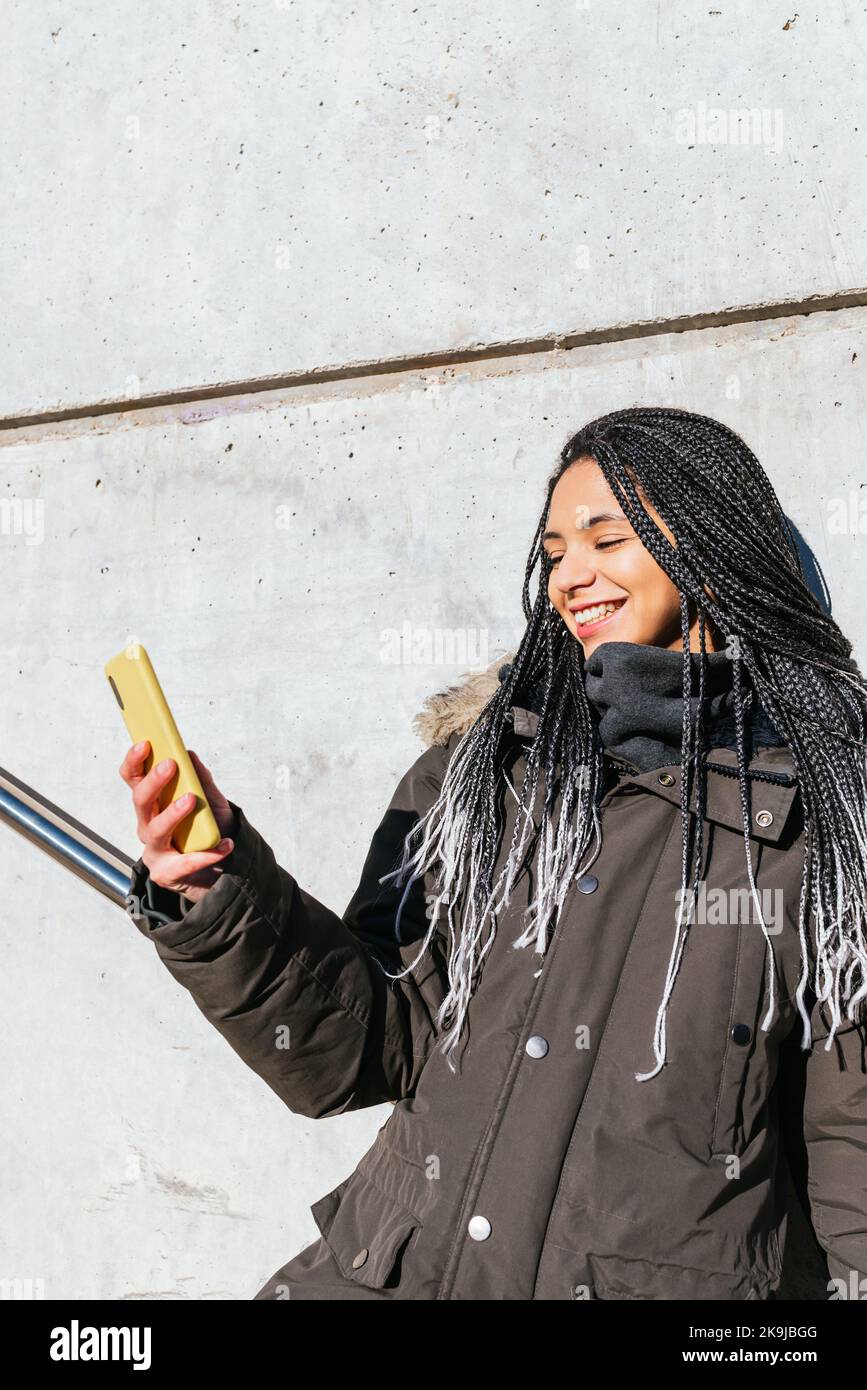 Delighted female with braids and in outerwear surfing internet on ...